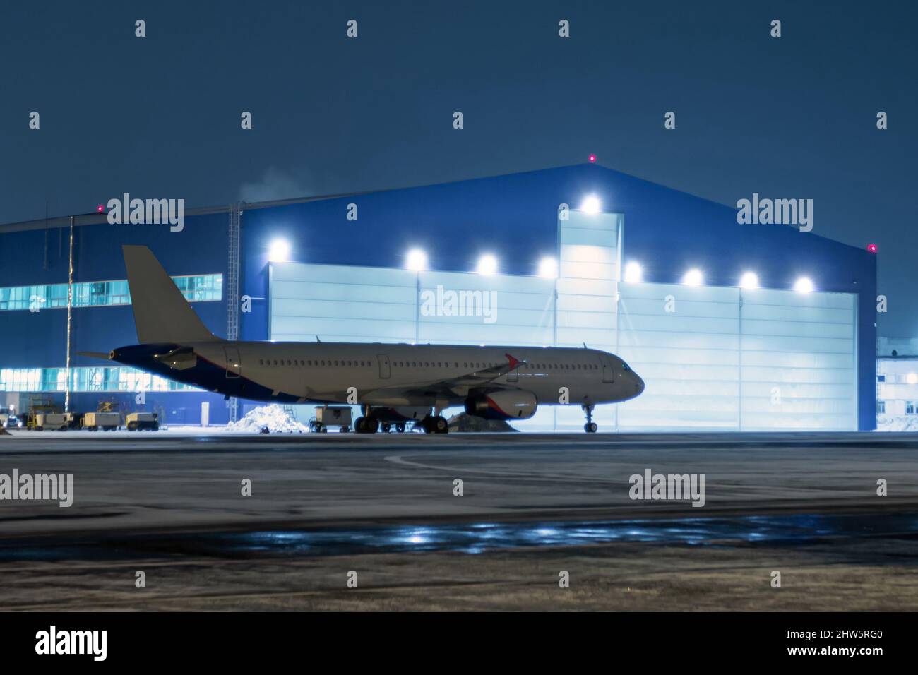 Passenger airplane at the parking lot near aviation hangar at night ...