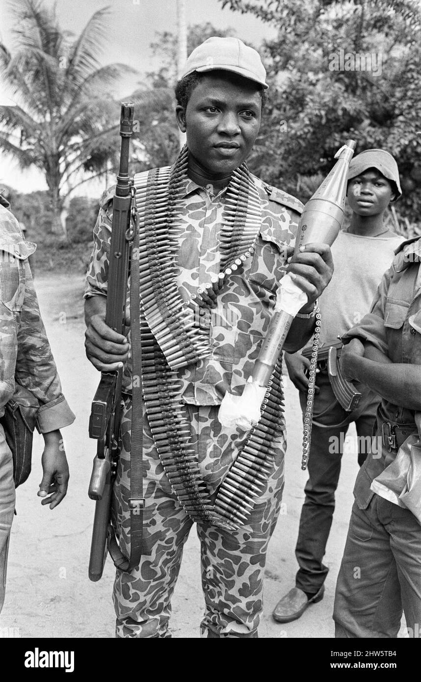 A Biafran soldier seen here holding an AK-47 assault rifle in one hand and a rocket propelled ...