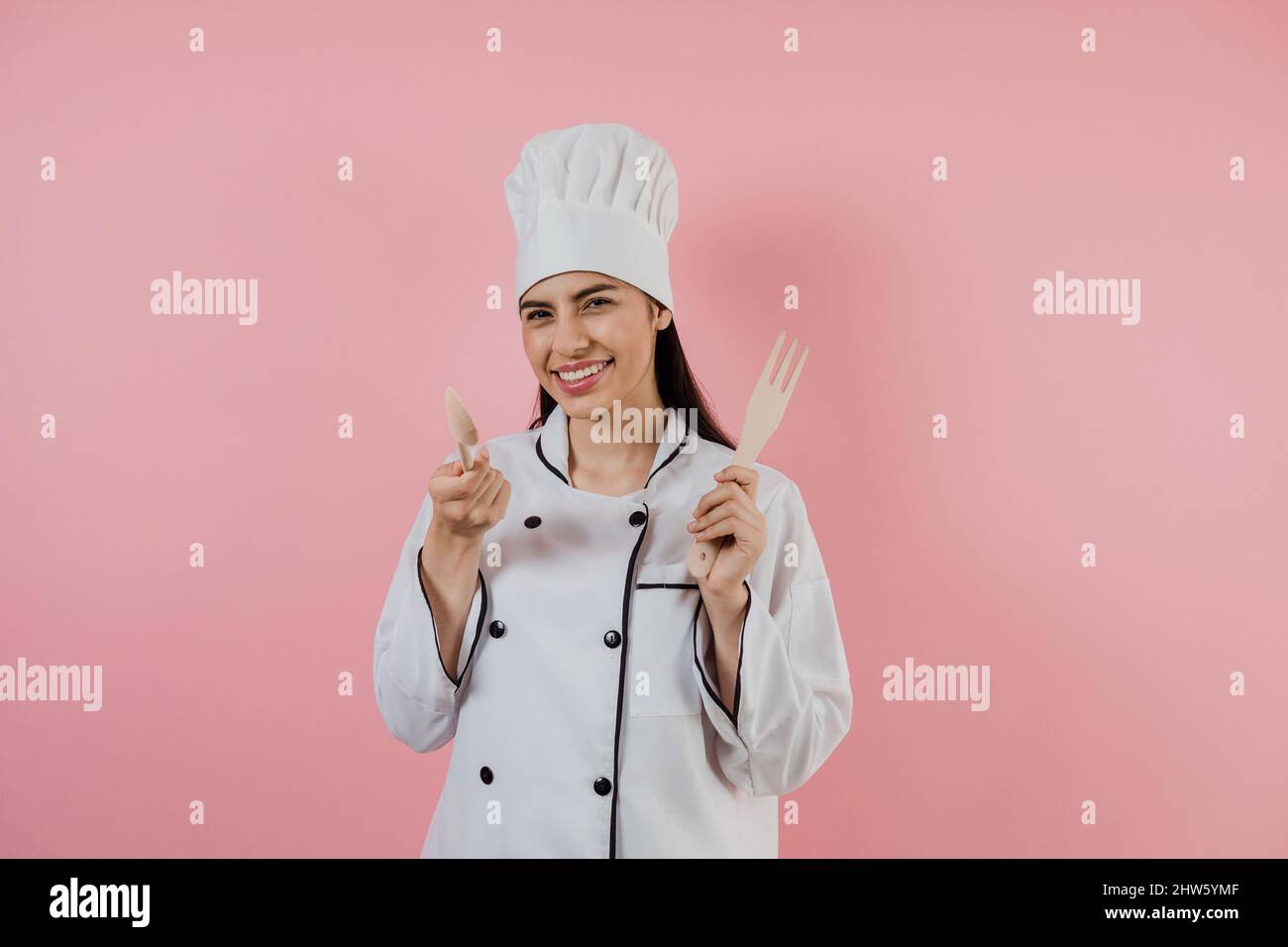 Portrait of young mexican woman chef or baker on pink background in ...