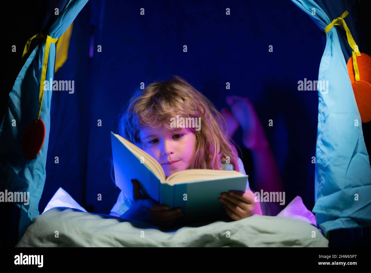 Kids reading a book in the dark home. Child boy reading a book lying on ...