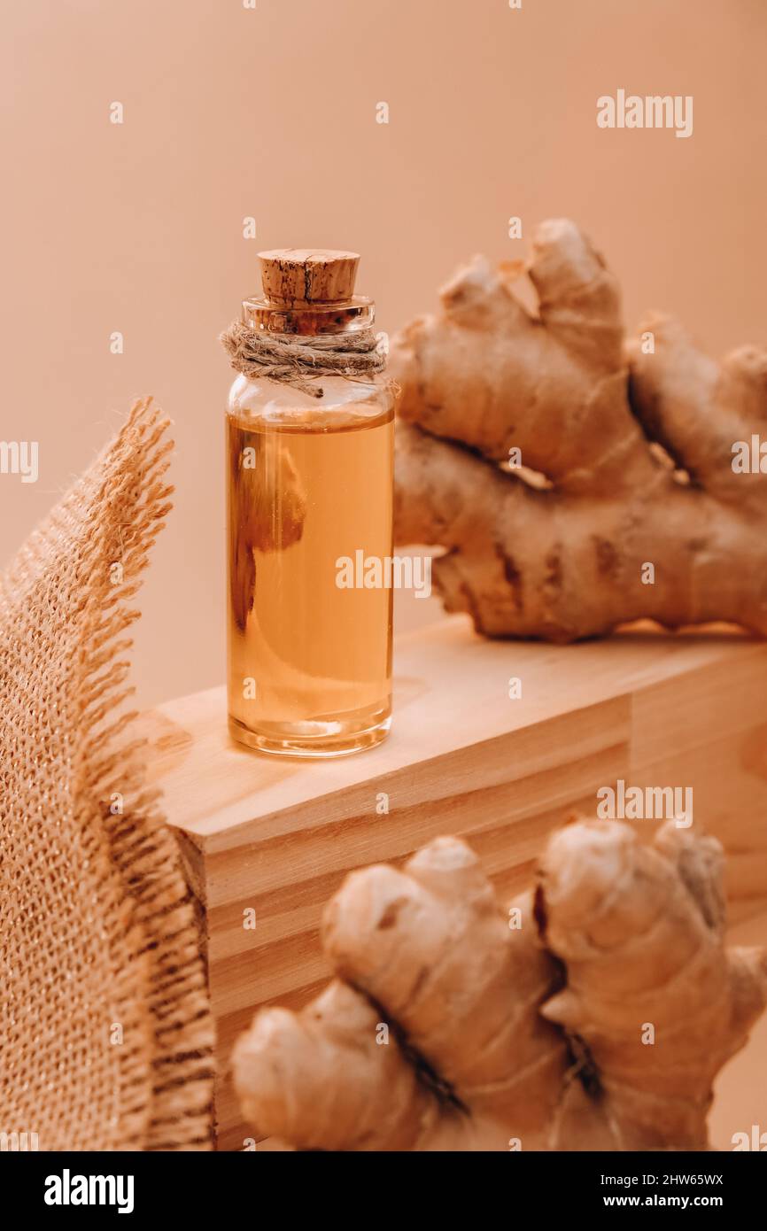 Glass bottle of essential ginger oil, ginger root on beige background ...