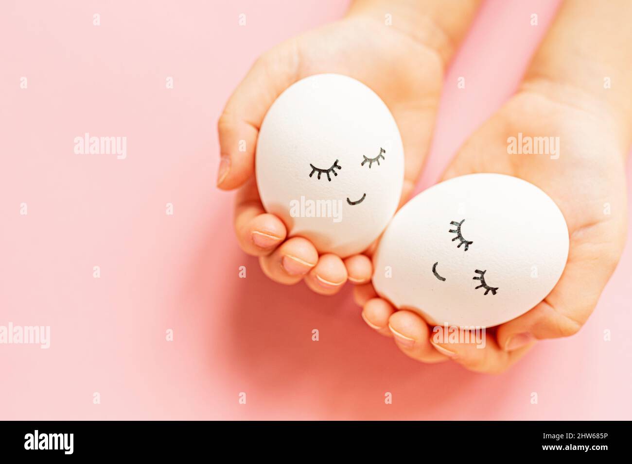 Hands holding easter eggs with cute face and sleepy eyes on pastel pink ...