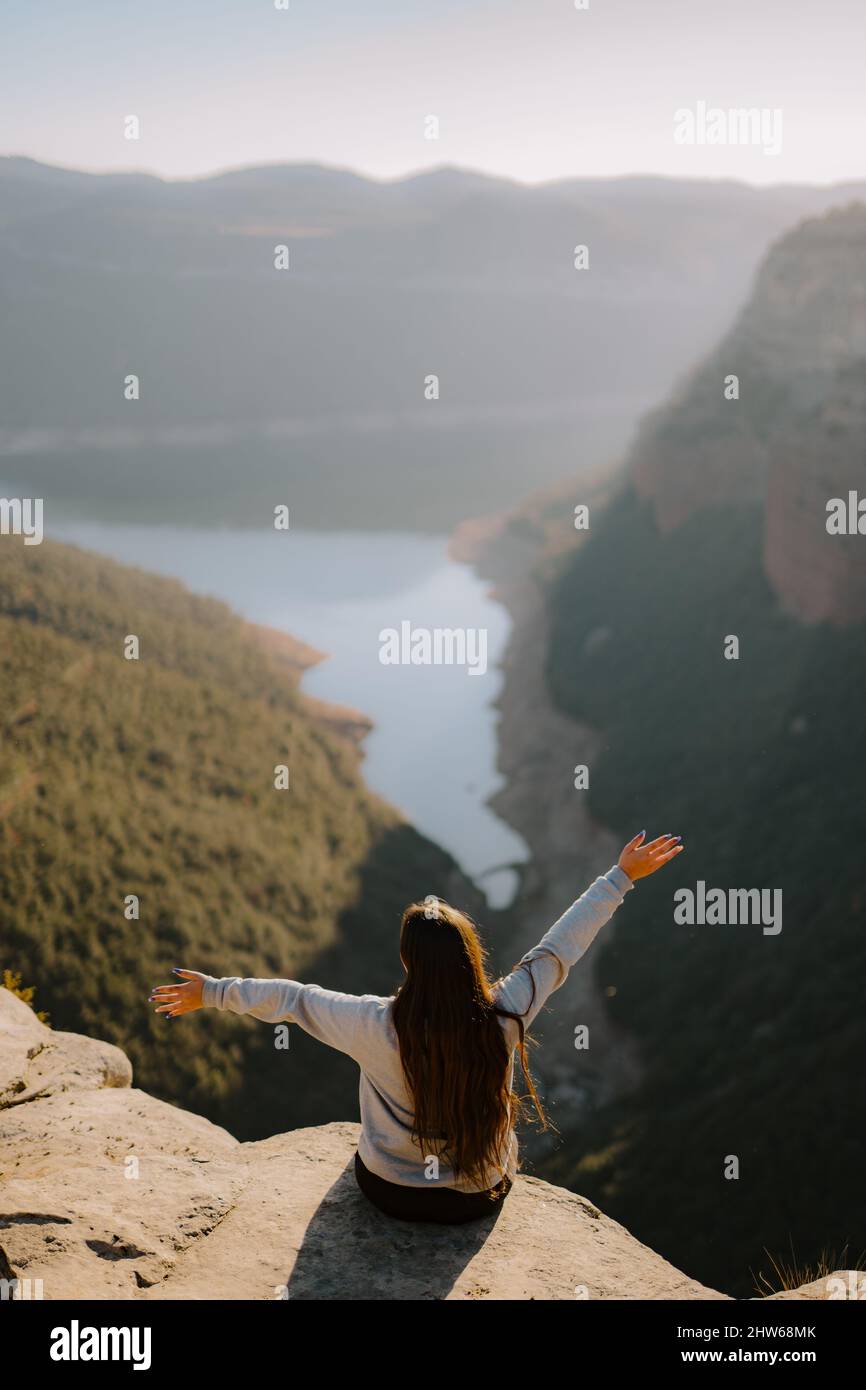 Vertical back view of a young girl sitting on a cliff edge in front of ...