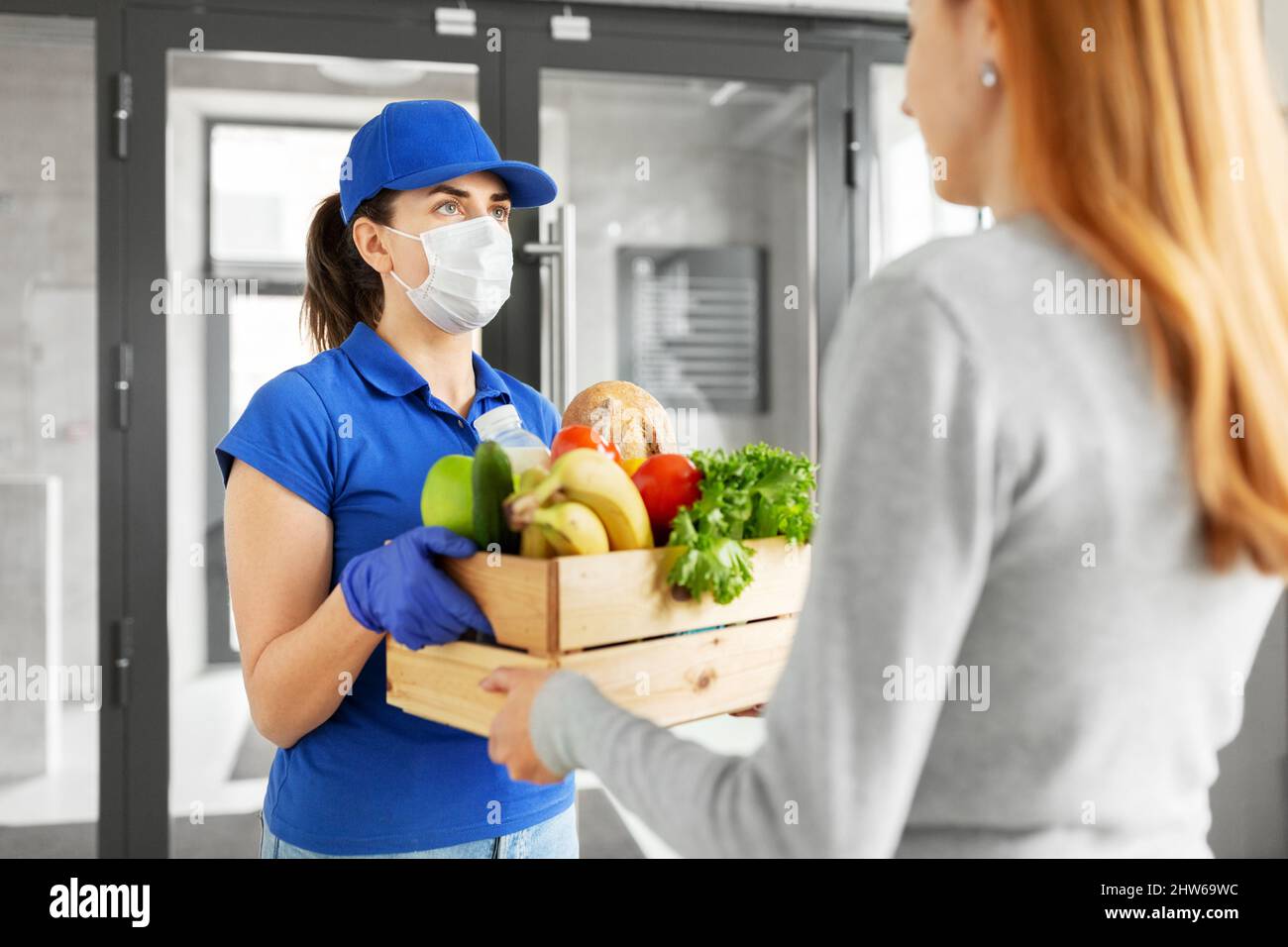 delivery girl in mask giving box of food to woman Stock Photo - Alamy