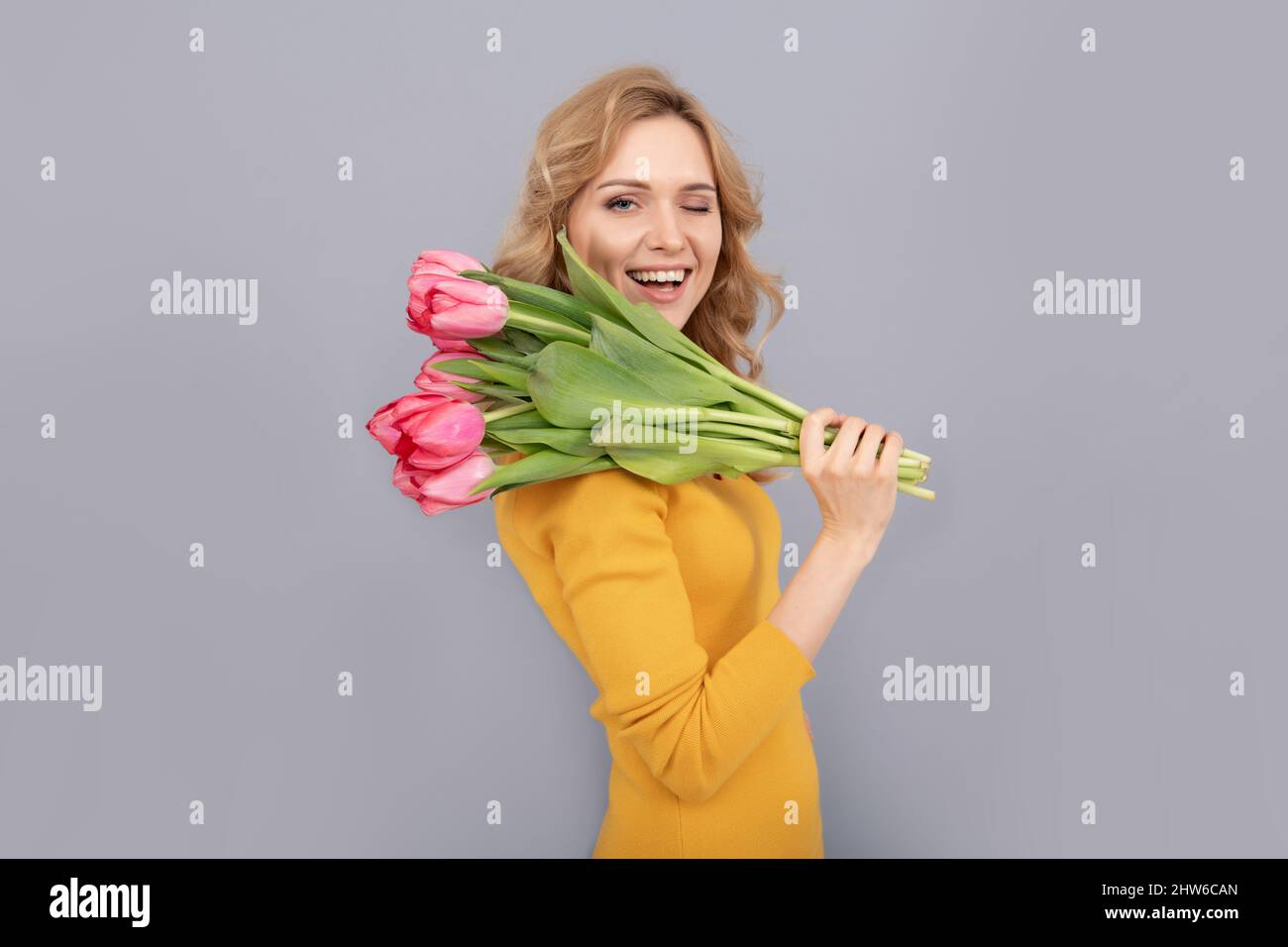 winking happy lady hold flowers for spring holiday on grey background ...