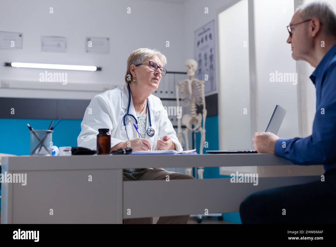 General practitioner consulting sick patient and preparing to sign ...