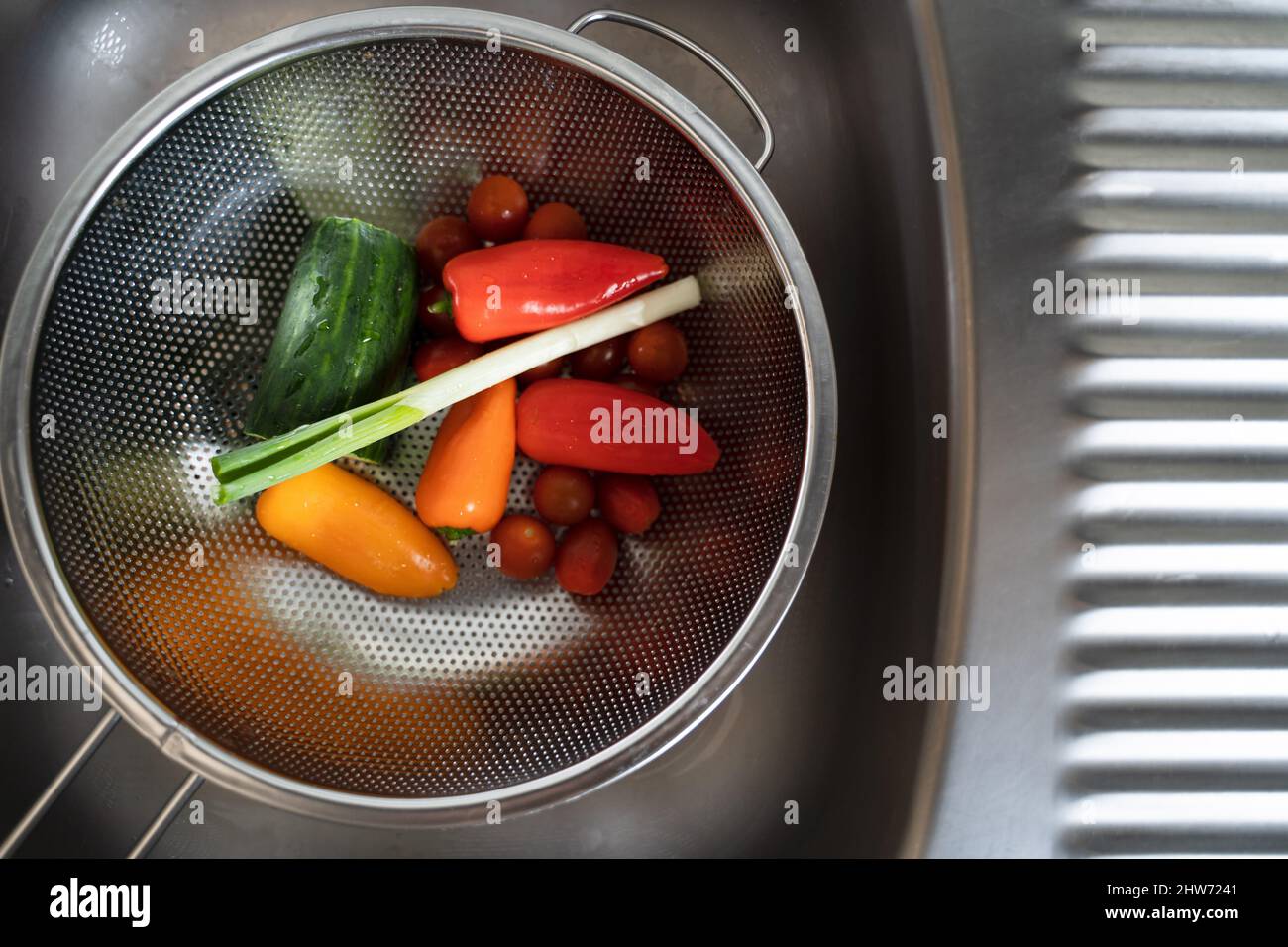 Cucumber tomato green onion and bell pepper in a strainer in the chrome ...