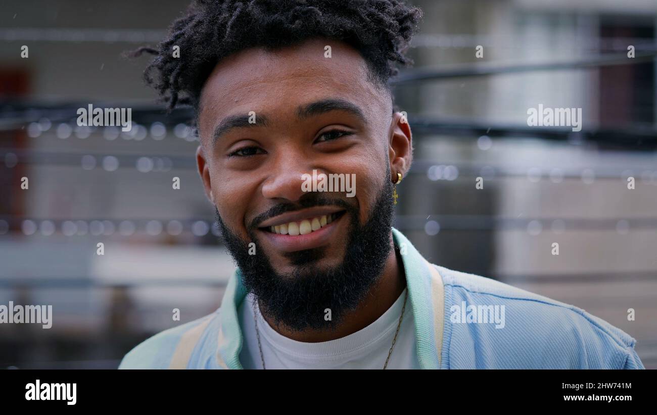 A happy young Brazilian man standing outside in drizzle smiling at ...