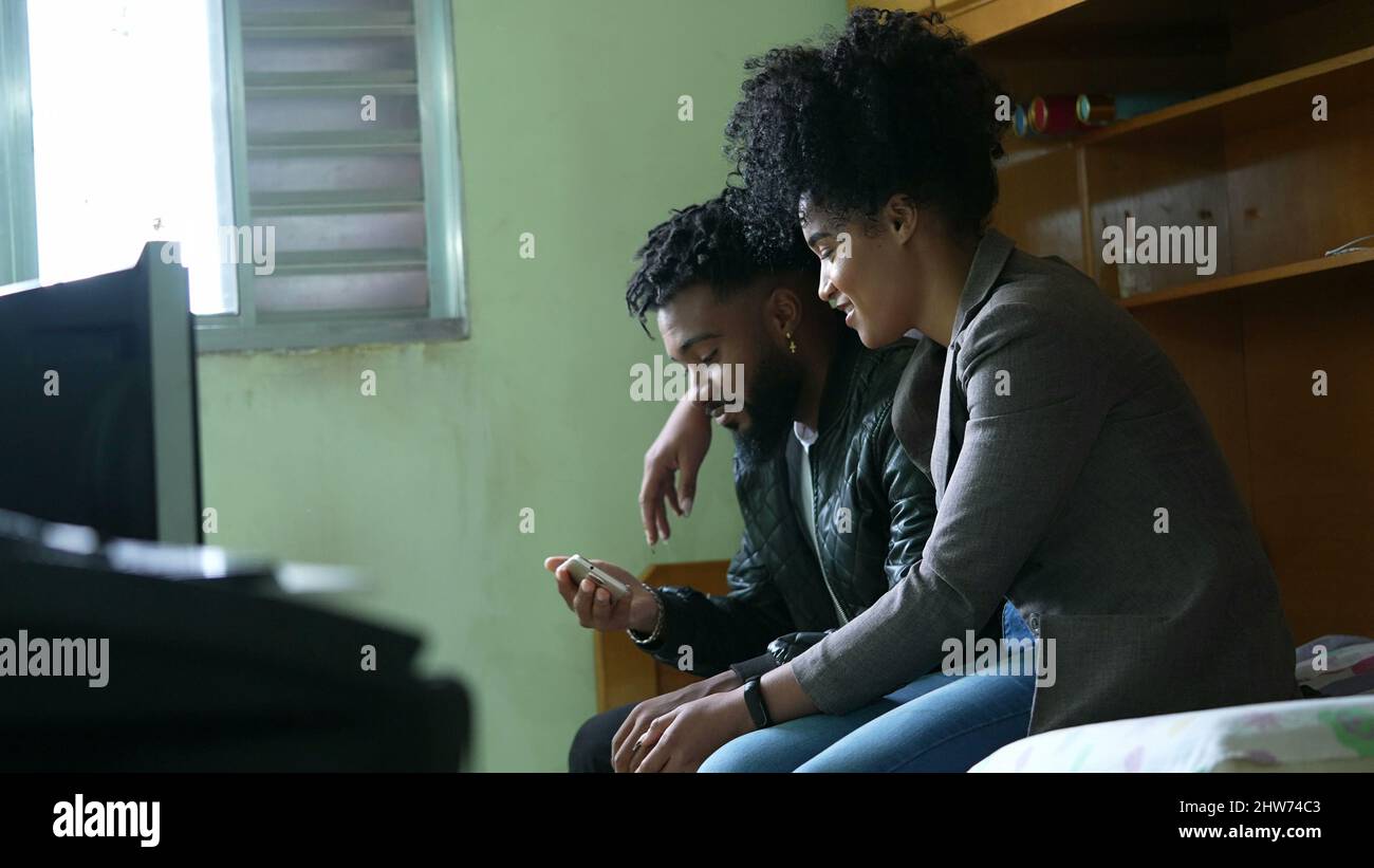 An African couple sitting together staring at cellphone device Stock ...