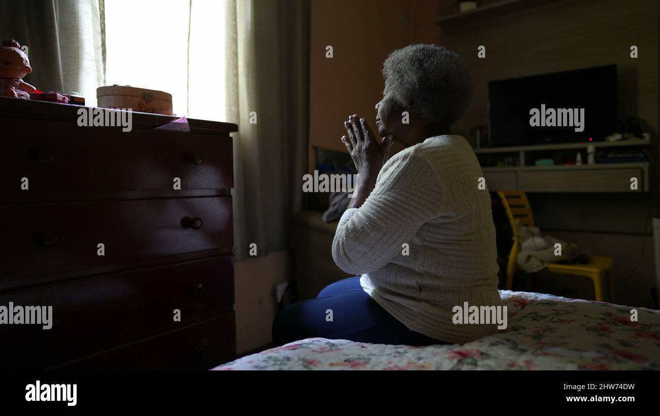 An older black woman praying by the bedside at home a religious person ...