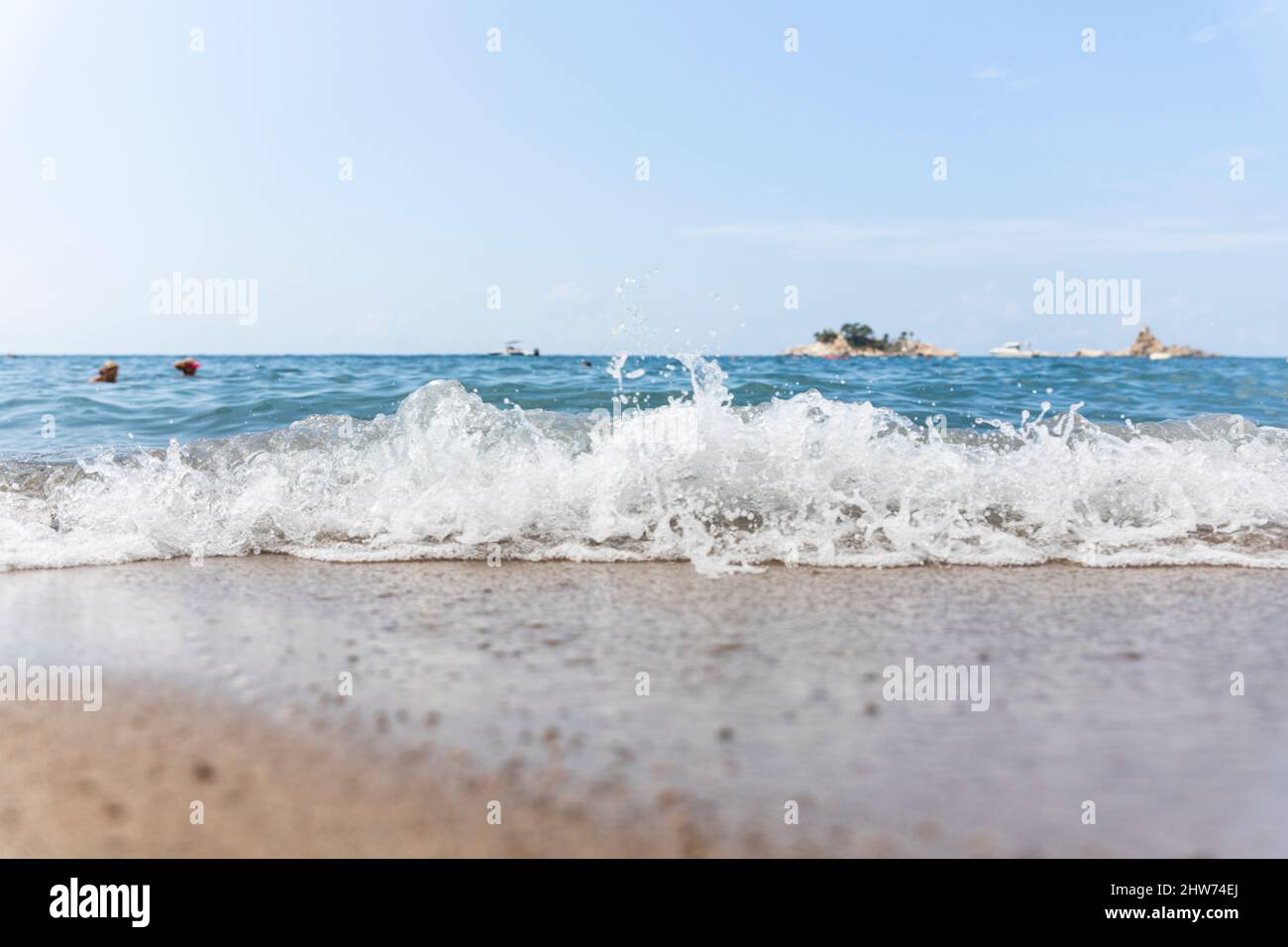 Waves splashing at sandy beach with swimmers and boats in the distance ...