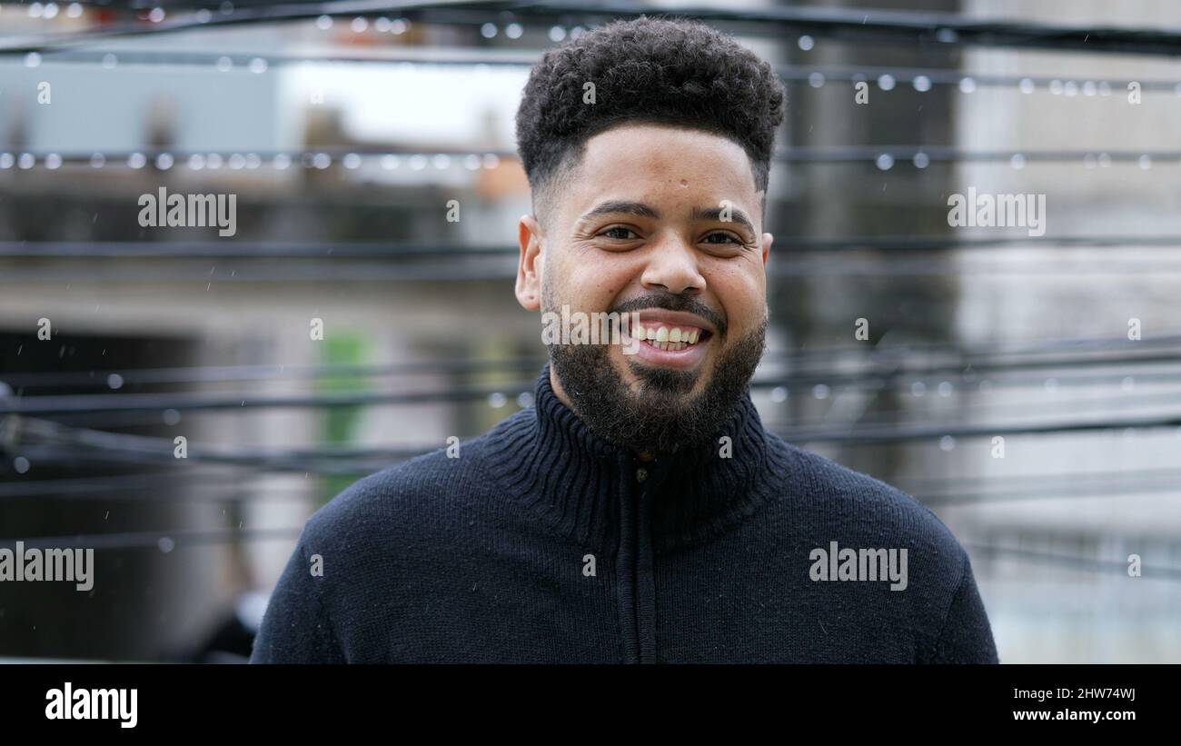 One young Brazilian man standing in the drizzle smiling at camera ...