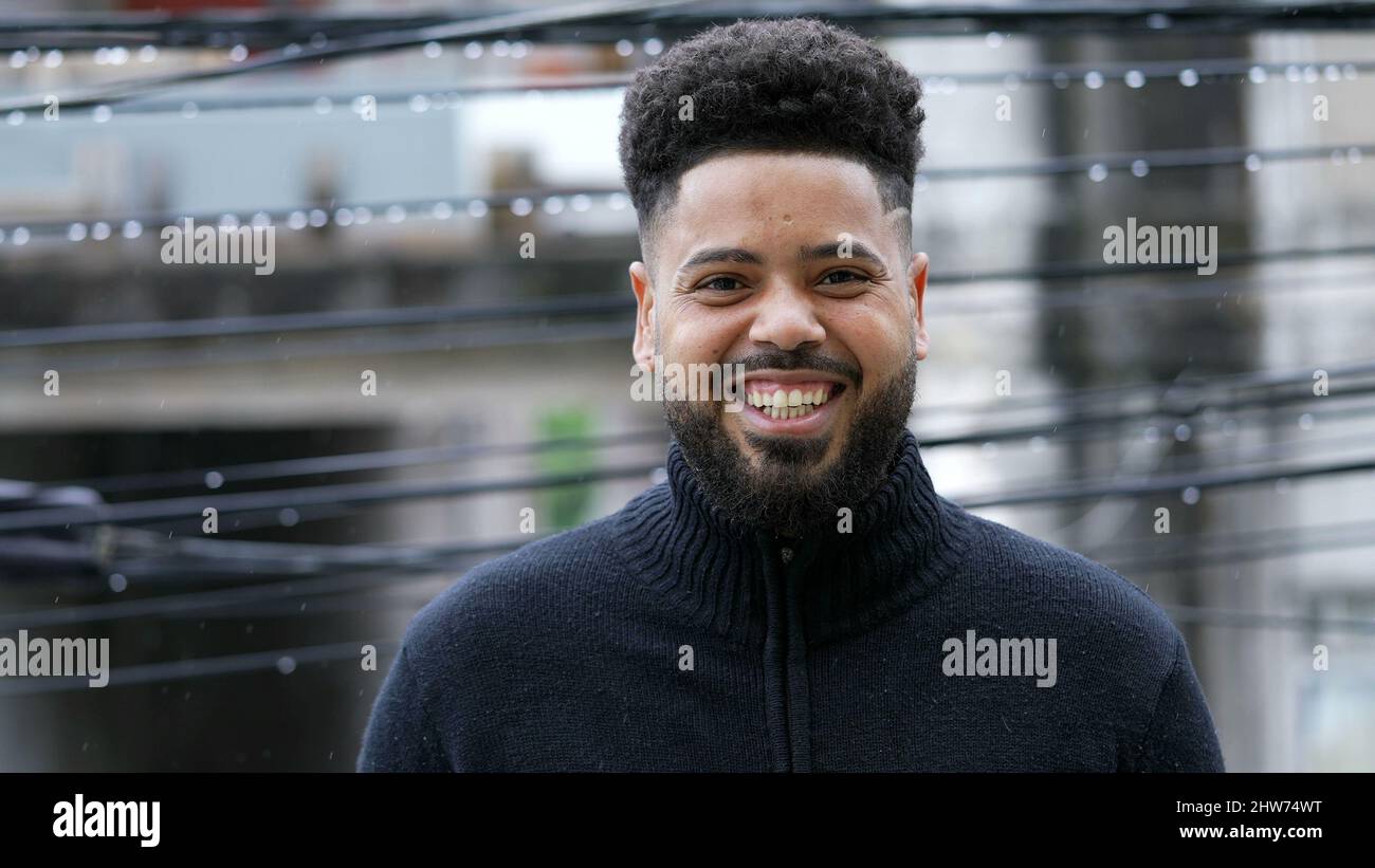 One young Brazilian man standing in the drizzle smiling at camera ...