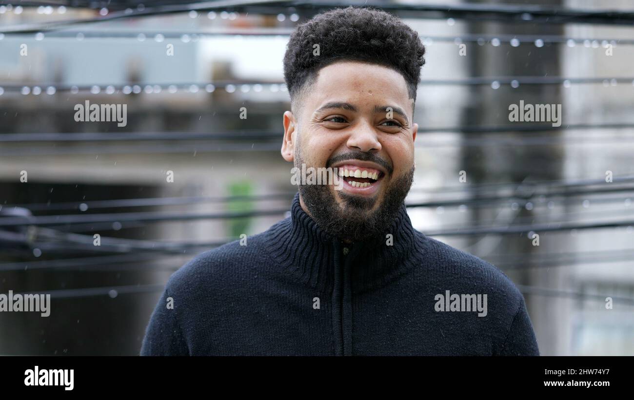 One young Brazilian man standing in the drizzle smiling at camera ...