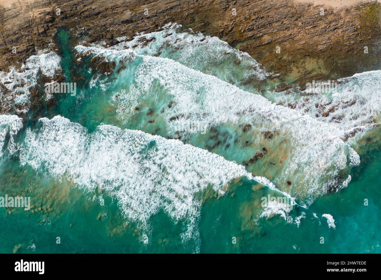 Aerial top down view of ocean waves crashing on rocky shore along the ...