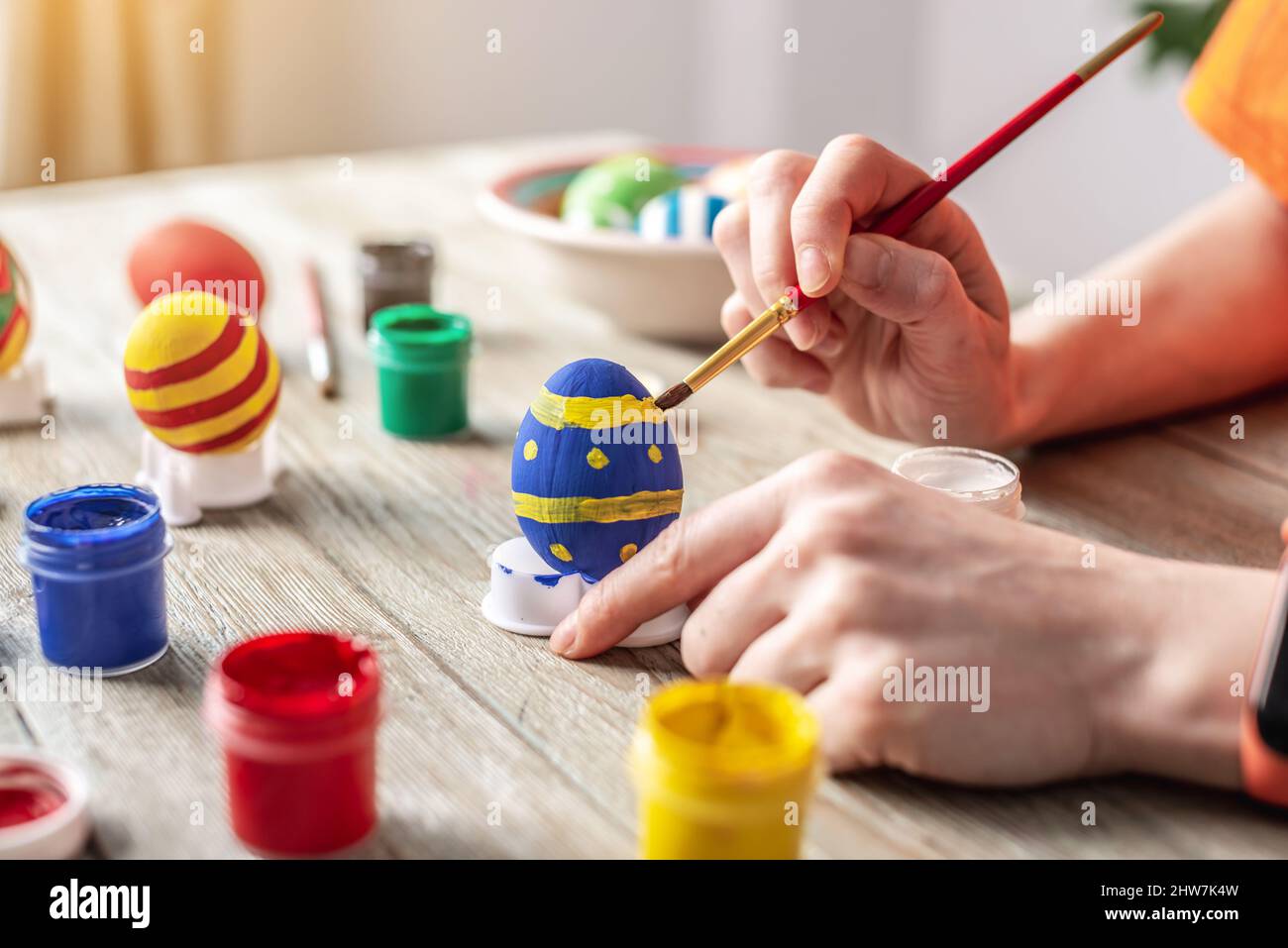 Woman's hand with a brush is drawing a colored pattern on an Easter egg ...
