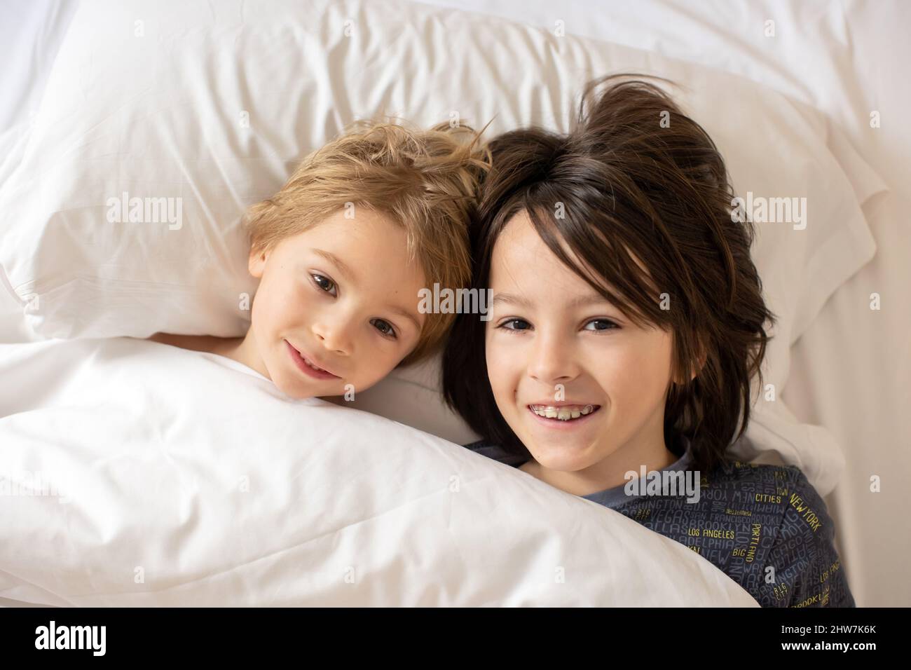 Two children, blond toddler boy and older brother, cuddling in bed in ...