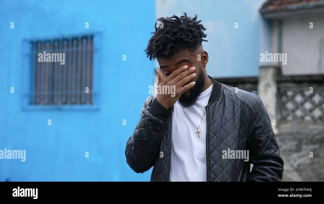 A tired black man rubbing eye and face outside Stock Photo - Alamy