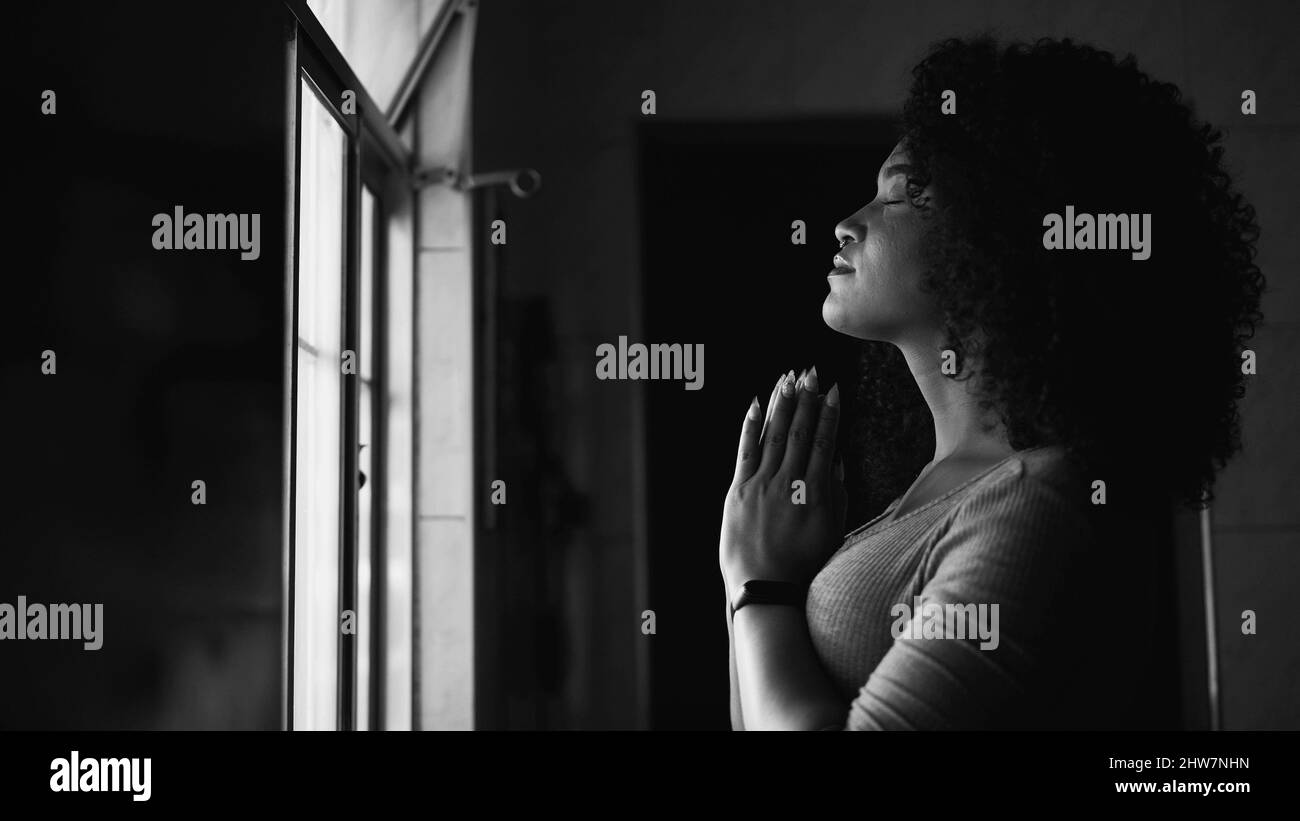A woman praying at home by window having HOPE and FAITH in monochrome ...