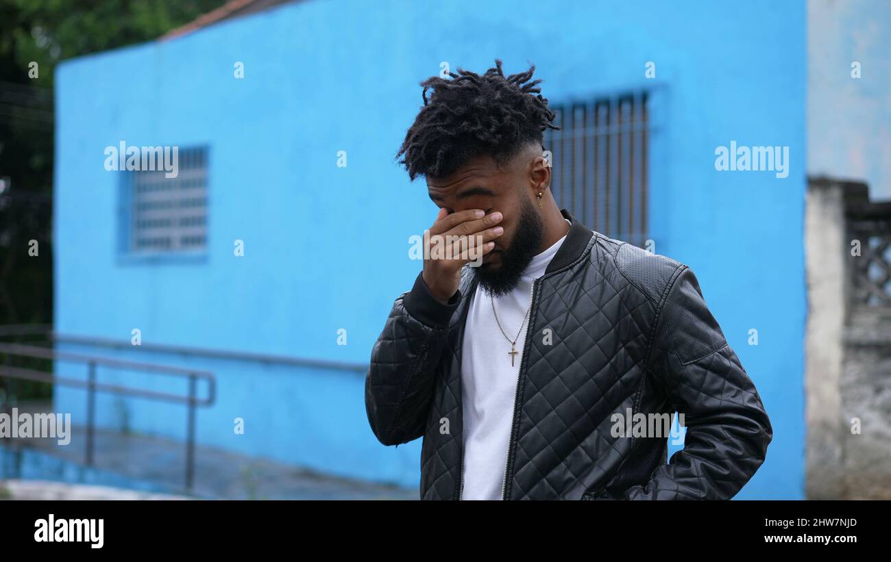 A tired black man rubbing eye and face outside Stock Photo - Alamy