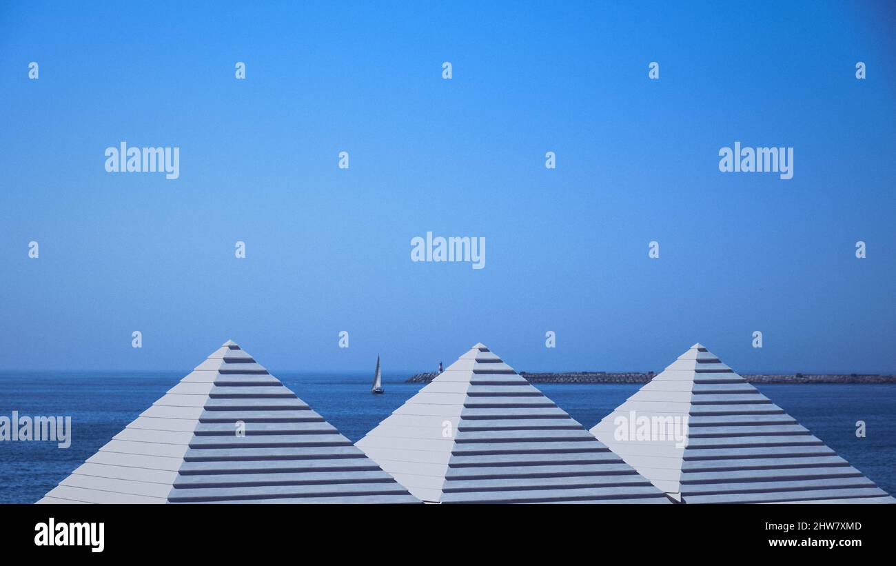 Triangle-shaped beach tents with a sailboat in the background on Barra ...
