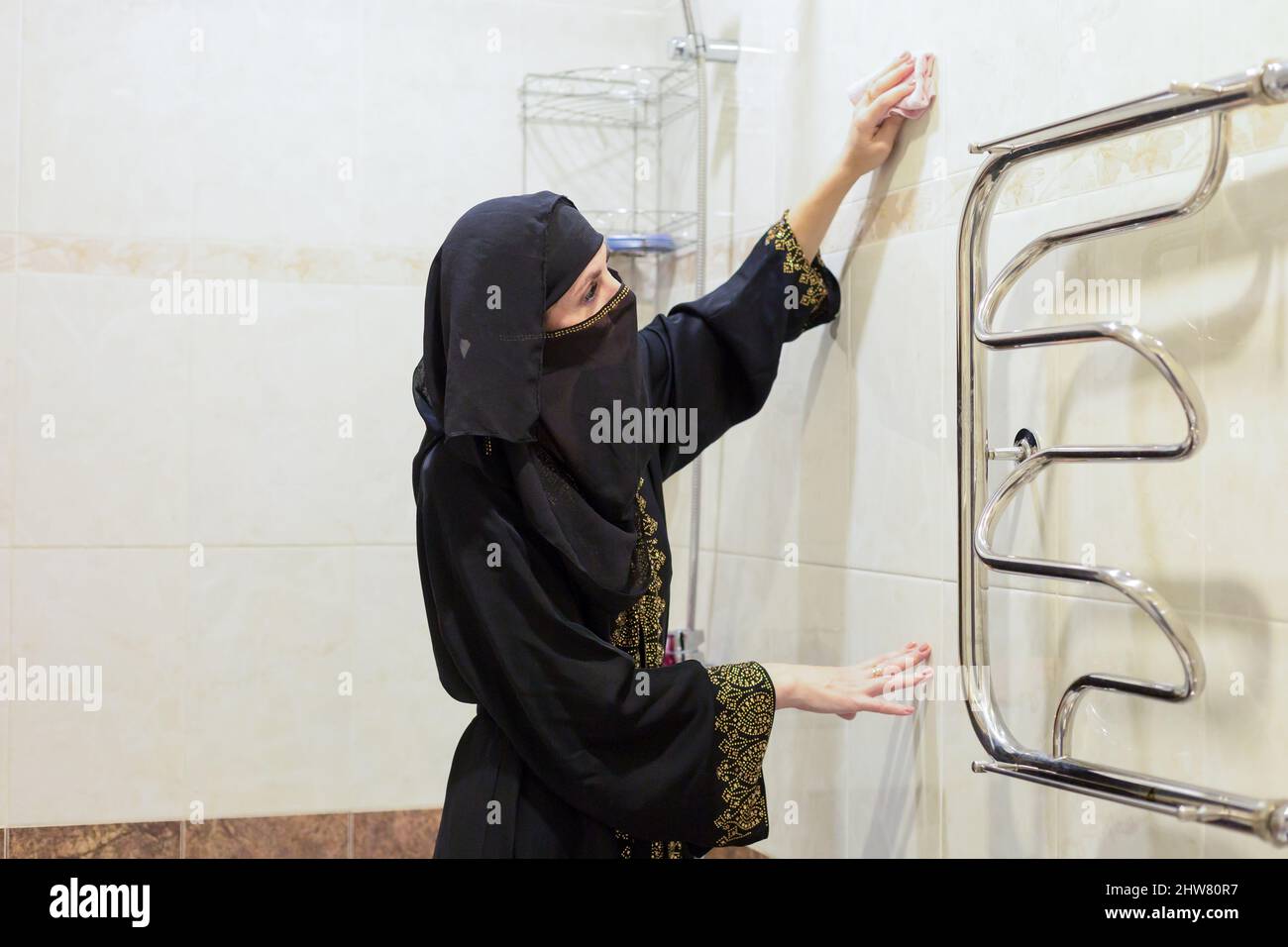 A Muslim woman in national clothes cleaning the bathroom washing the ...