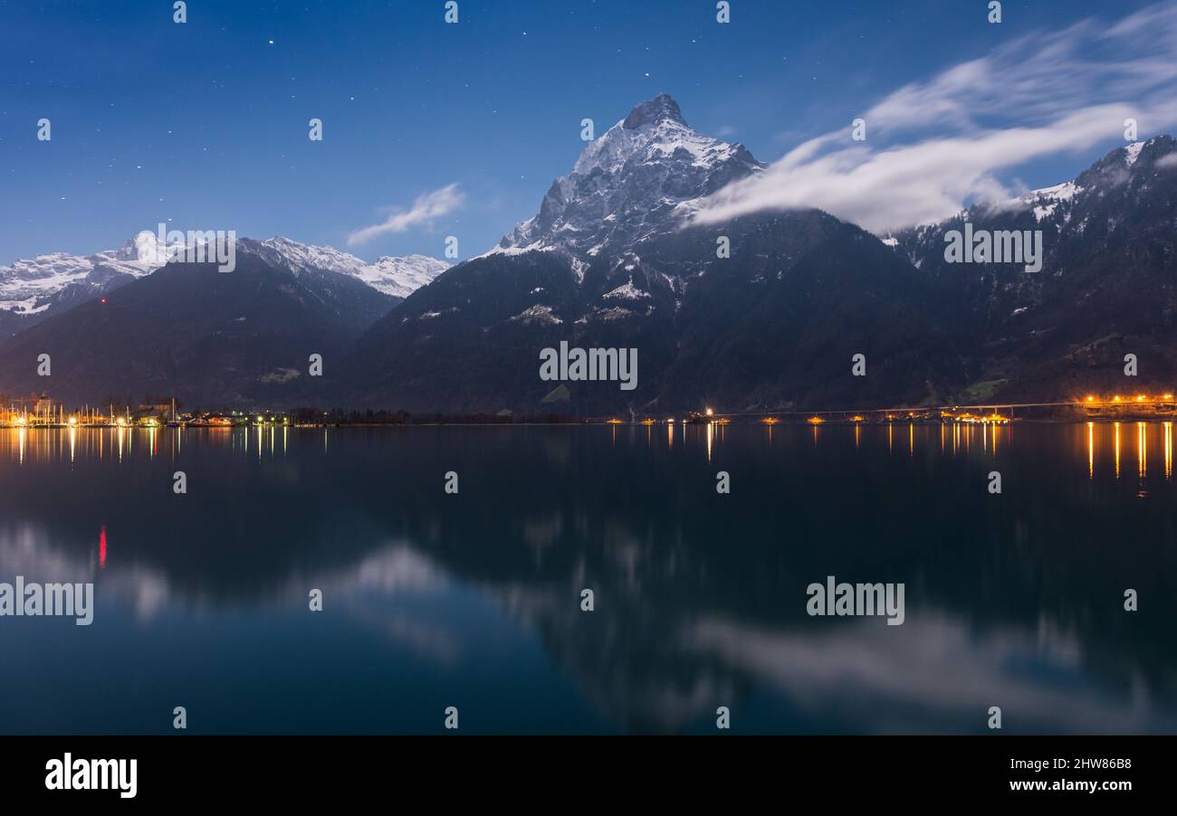 Night landscape. Swiss Alps in snow cover. City lights are reflected in ...
