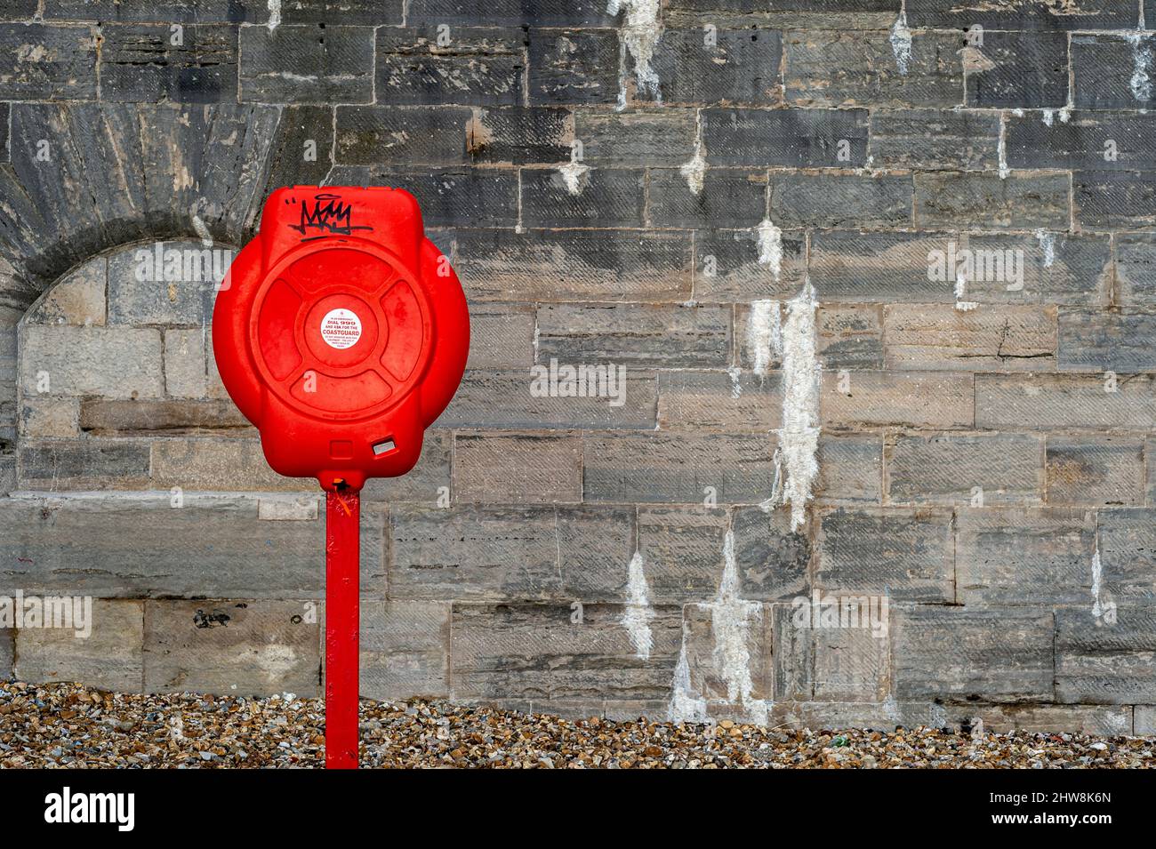 Red life bouy by a stone wall on a shingle beach Stock Photo - Alamy