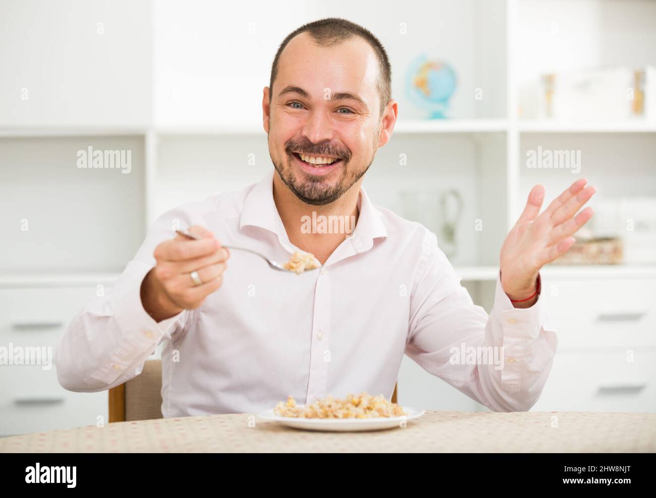 Positive young man eating porridge Stock Photo - Alamy