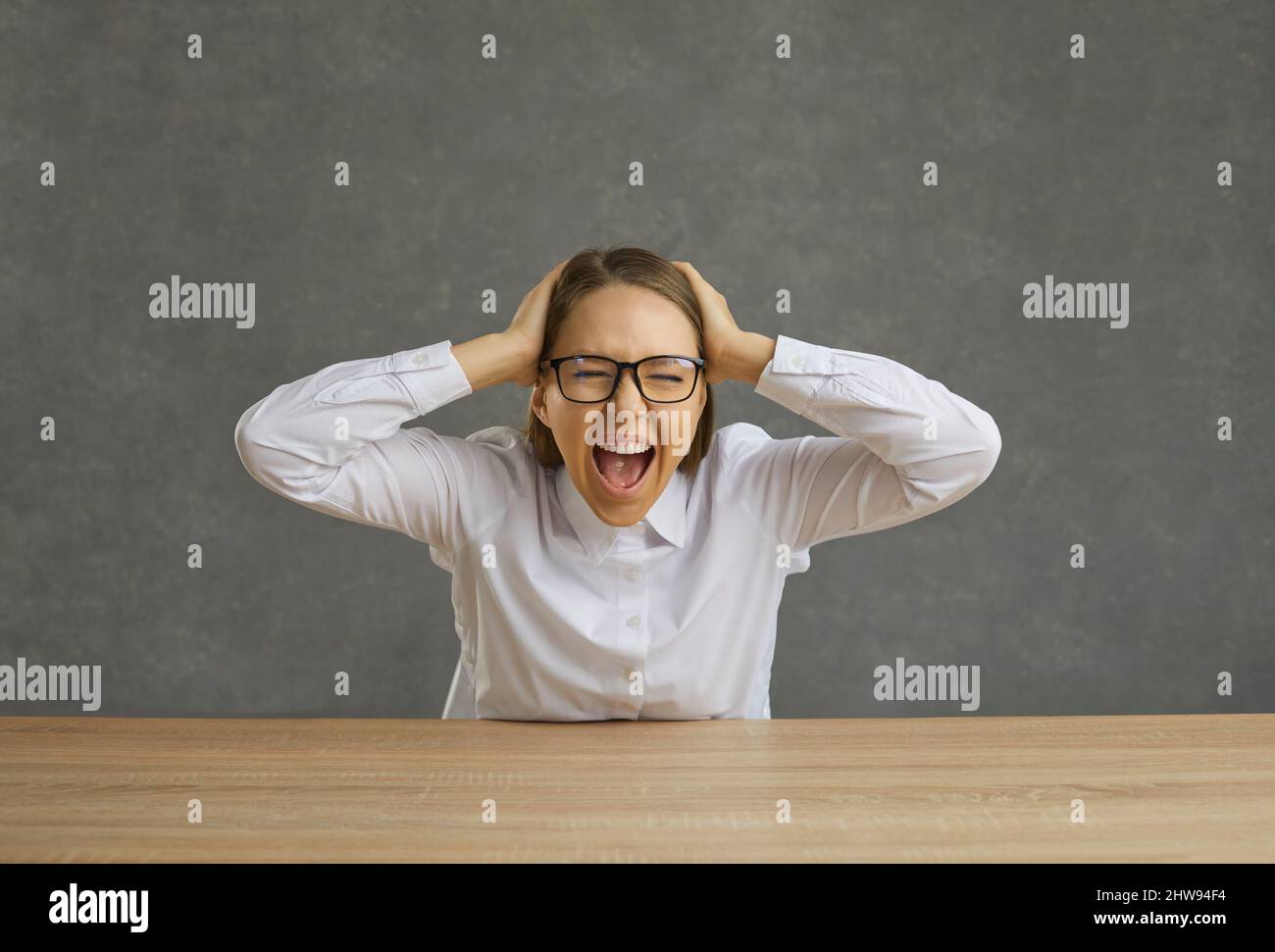 Portrait of angry stressed young woman sitting at desk, holding her ...