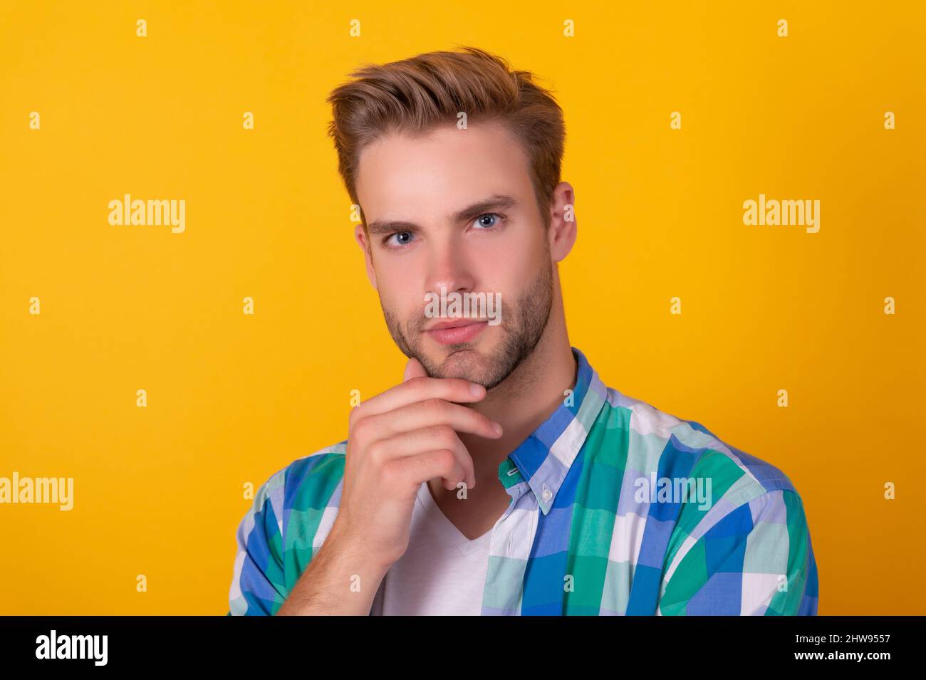 Handsome unshaven man portrait stroking chin with serious look yellow ...