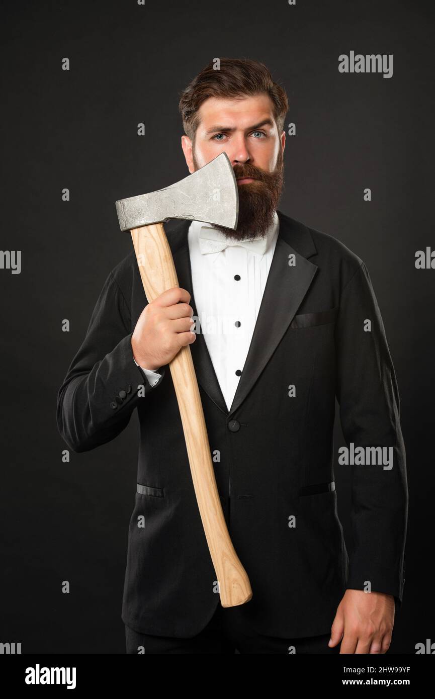 Serious bearded man in formal suit holding hatchet at unshaven face ...