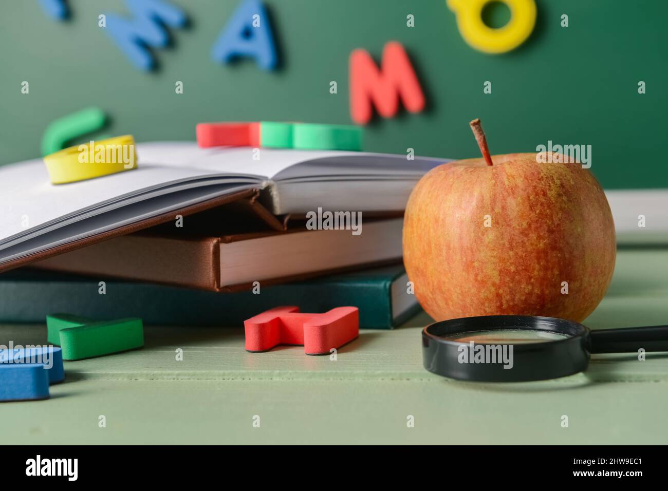 Books, magnifier, apple and colorful letters on table in classroom ...