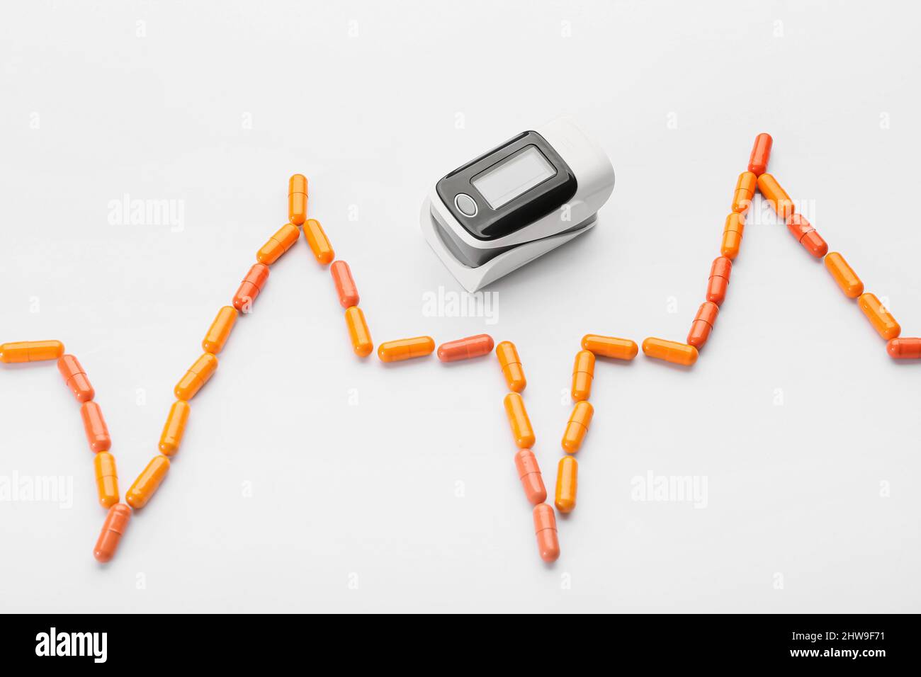 Cardiogram made of orange pills and pulse oximeter on white background ...