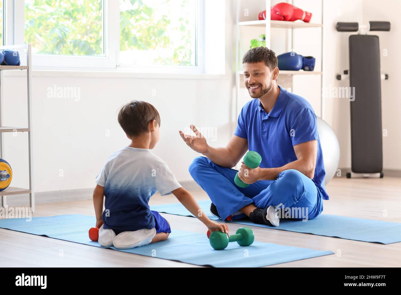 Male trainer with dumbbell and little boy in gym Stock Photo - Alamy