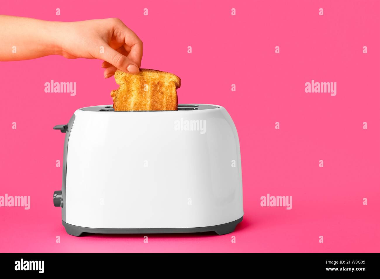 Woman taking bread slice from toaster on pink background Stock Photo - Alamy