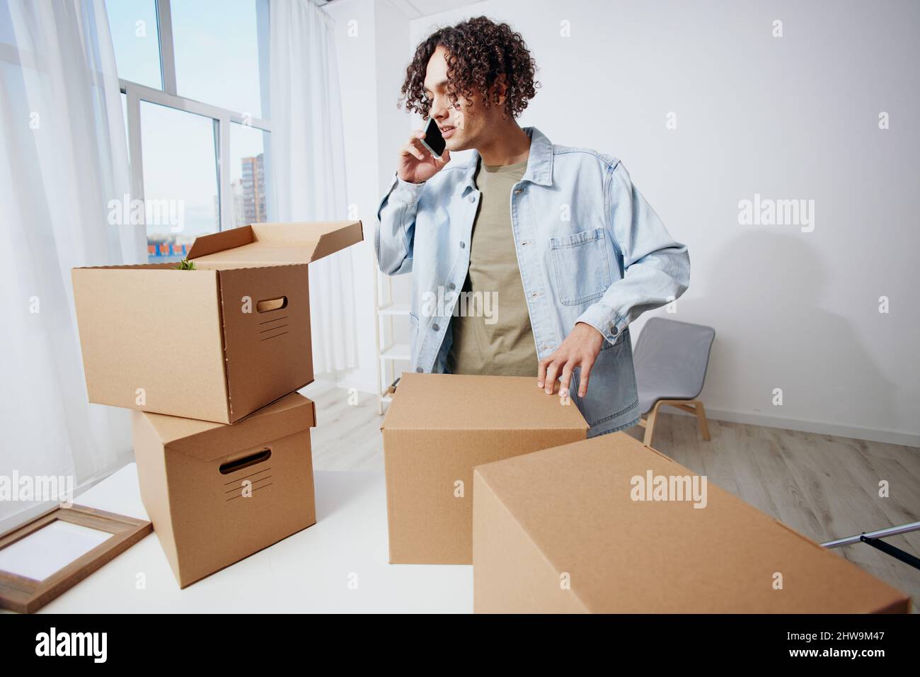 A young man unpacking things from boxes in the room sorting things out ...