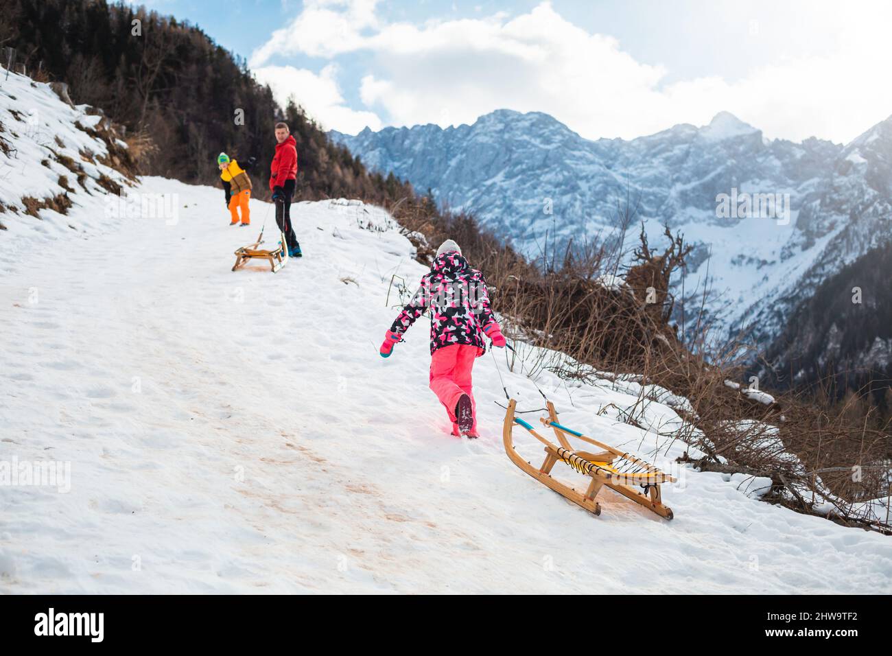 Man and two children in colorful snowsuits pulling wooden sleds on the ...