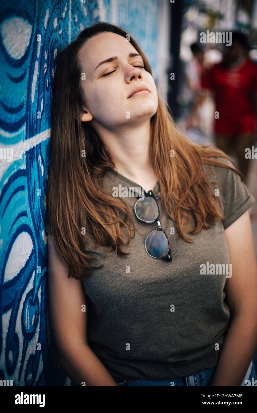 Young and beautiful woman leans against a colorful wall and poses for ...