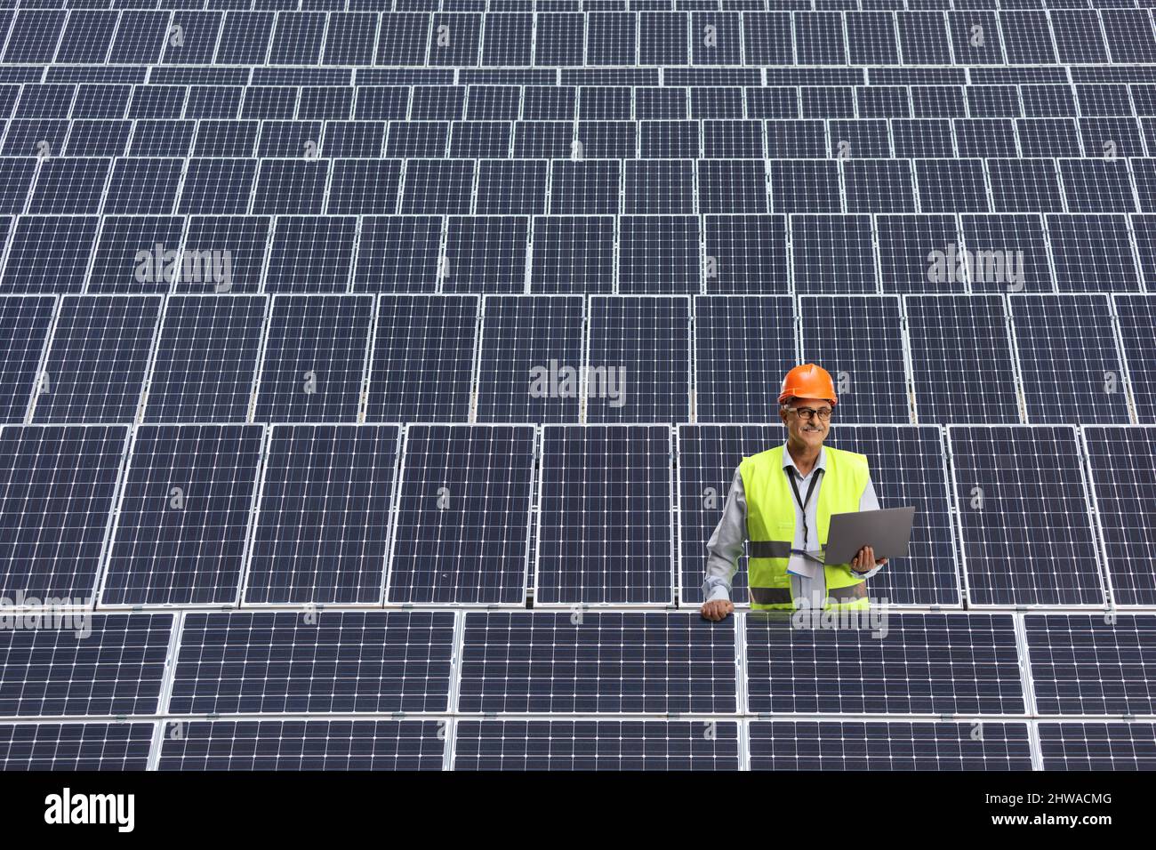Male engineer with a reflective vest standing between many solar cells ...