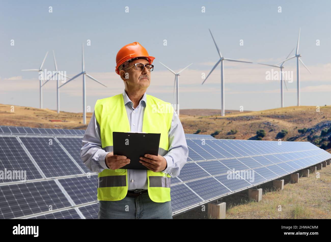 Mature male engineer standing on a field with solar panels and wind ...