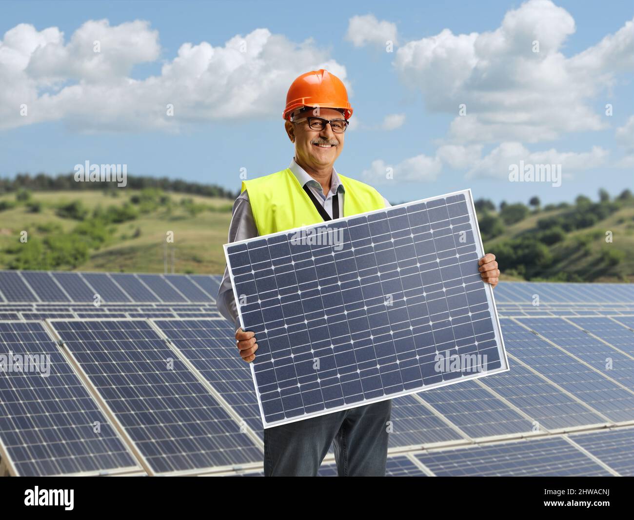 Male engineer with a reflective vest holding a solar panel in a field ...