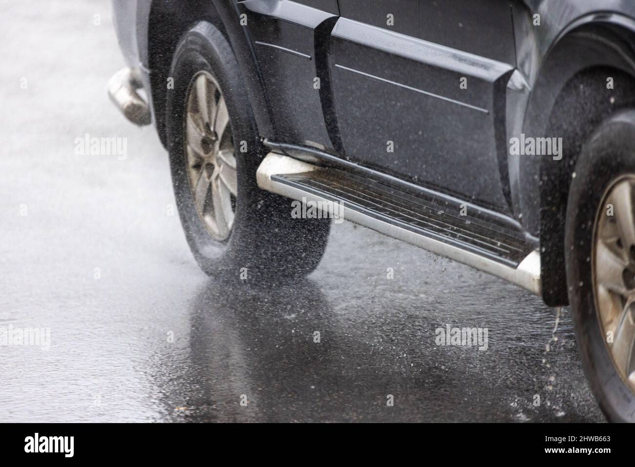 rain water splash flow from wheels of black car moving fast in daylight ...