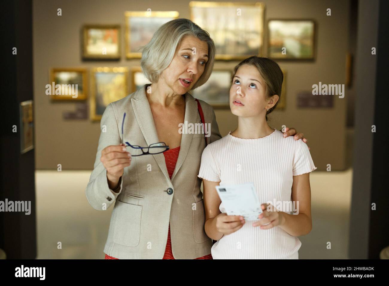 Attentive tween girl with senior woman looking with interest at gallery ...