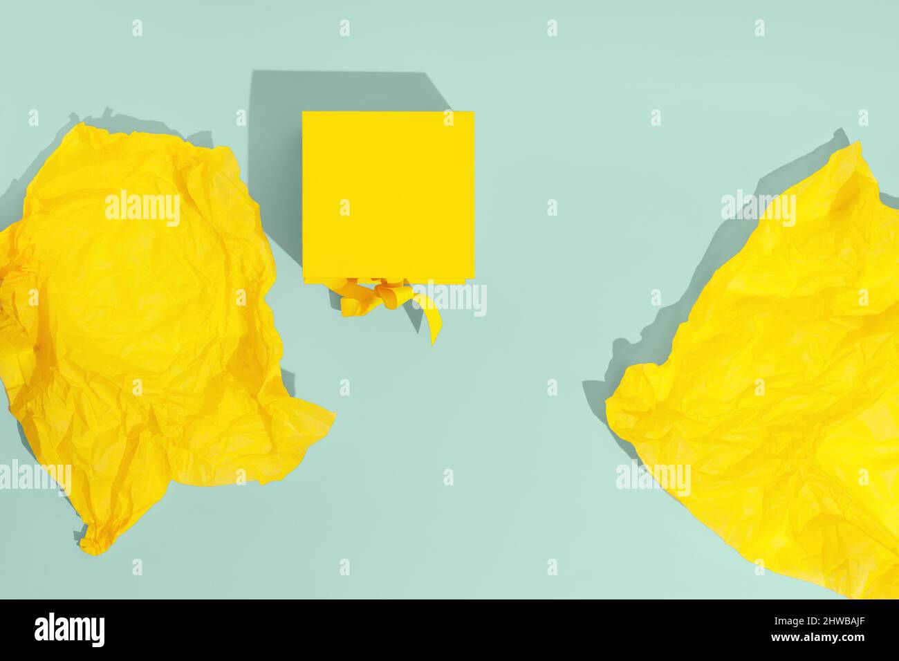 Bright yellow gift box with ribbon bow and wrapping paper on light blue ...