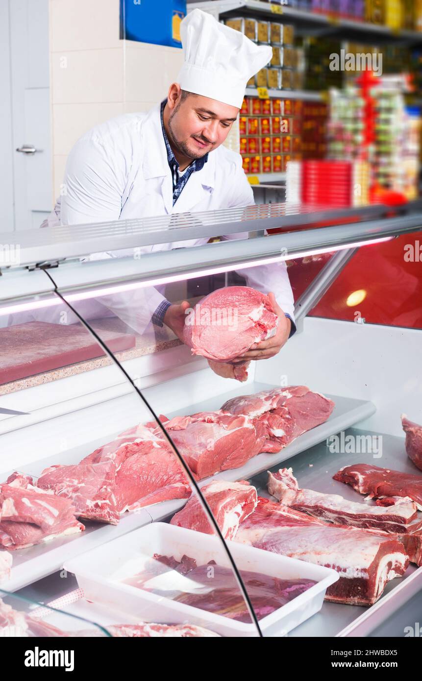 Portrait of professional positive butcher cutting fresh lamb meat in ...