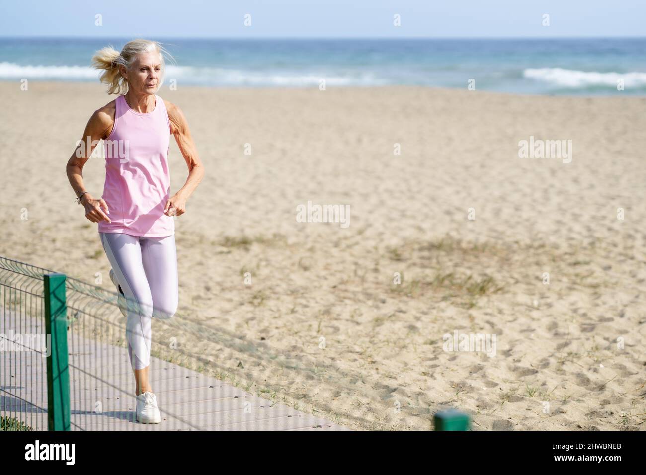 Older female doing sport to keep fit. Mature woman running along the shore of the beach Stock ...