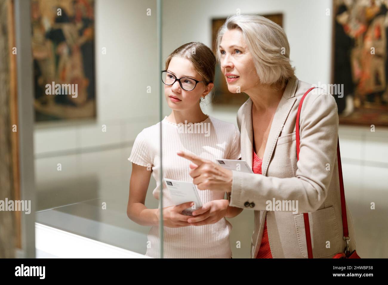 Attentive tween girl with senior woman looking with interest at gallery ...