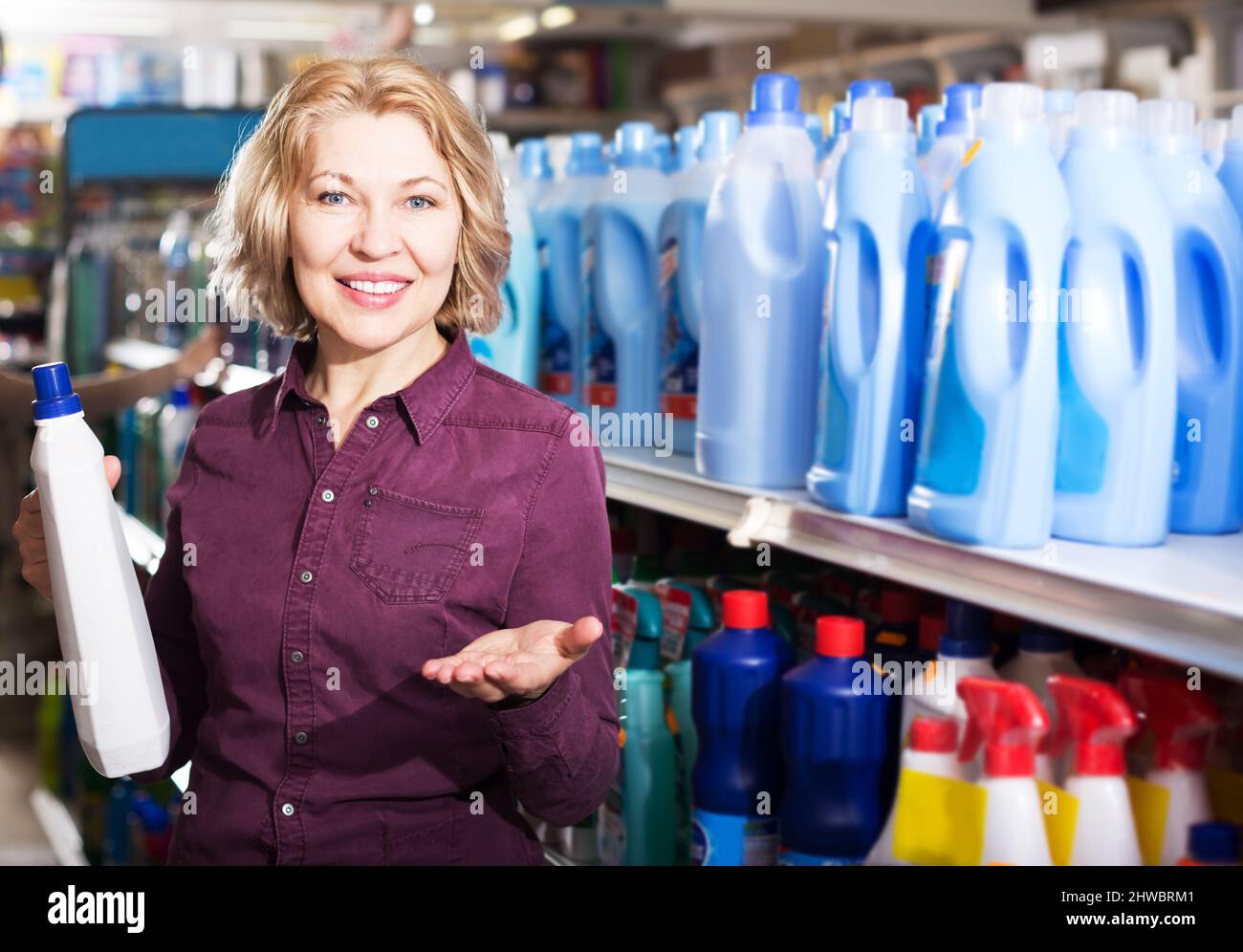 Aged blonde woman choosing detergent in laundry section of supermarket ...