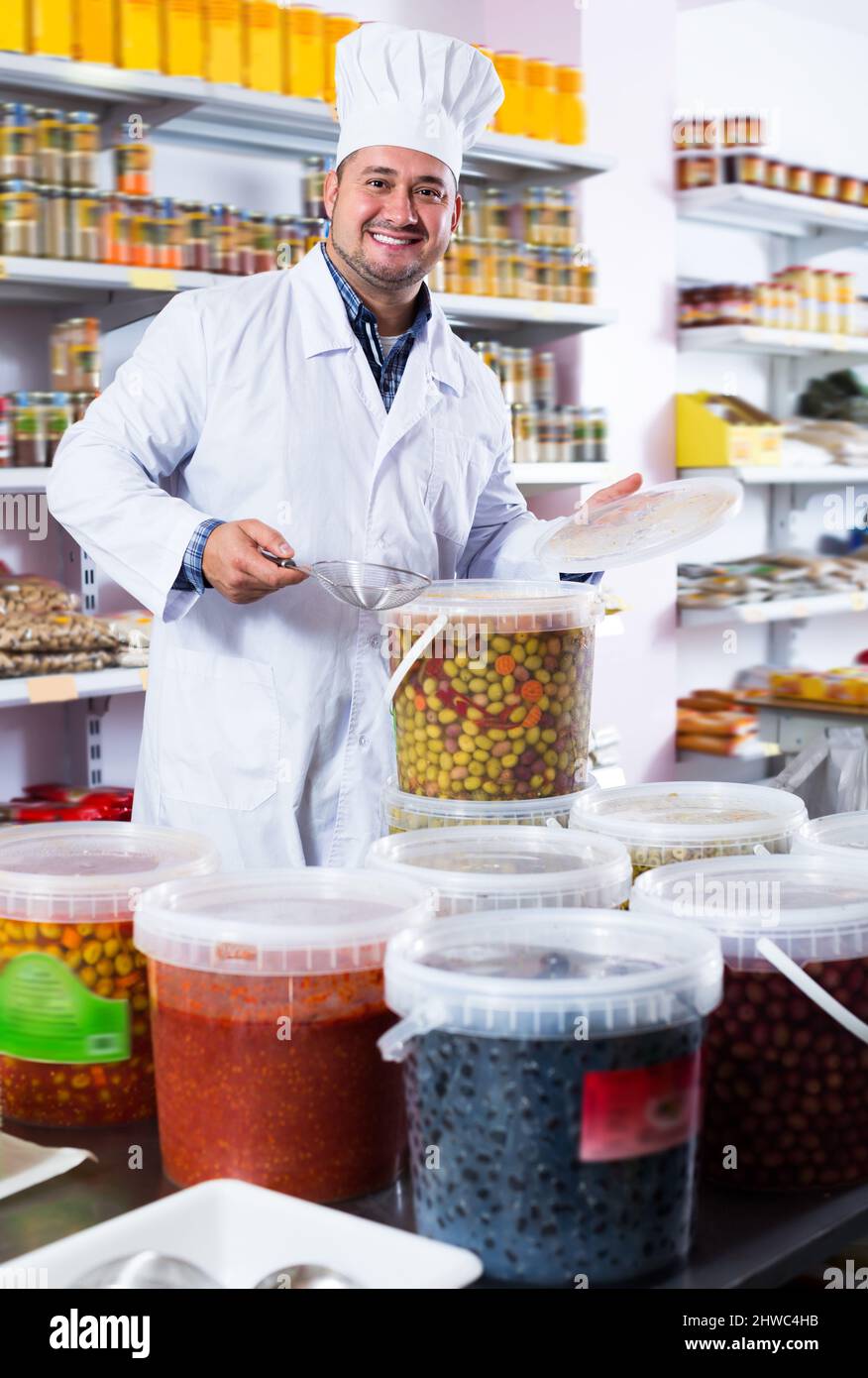 Salesman offering salted olives with filling in ordinary food shop ...
